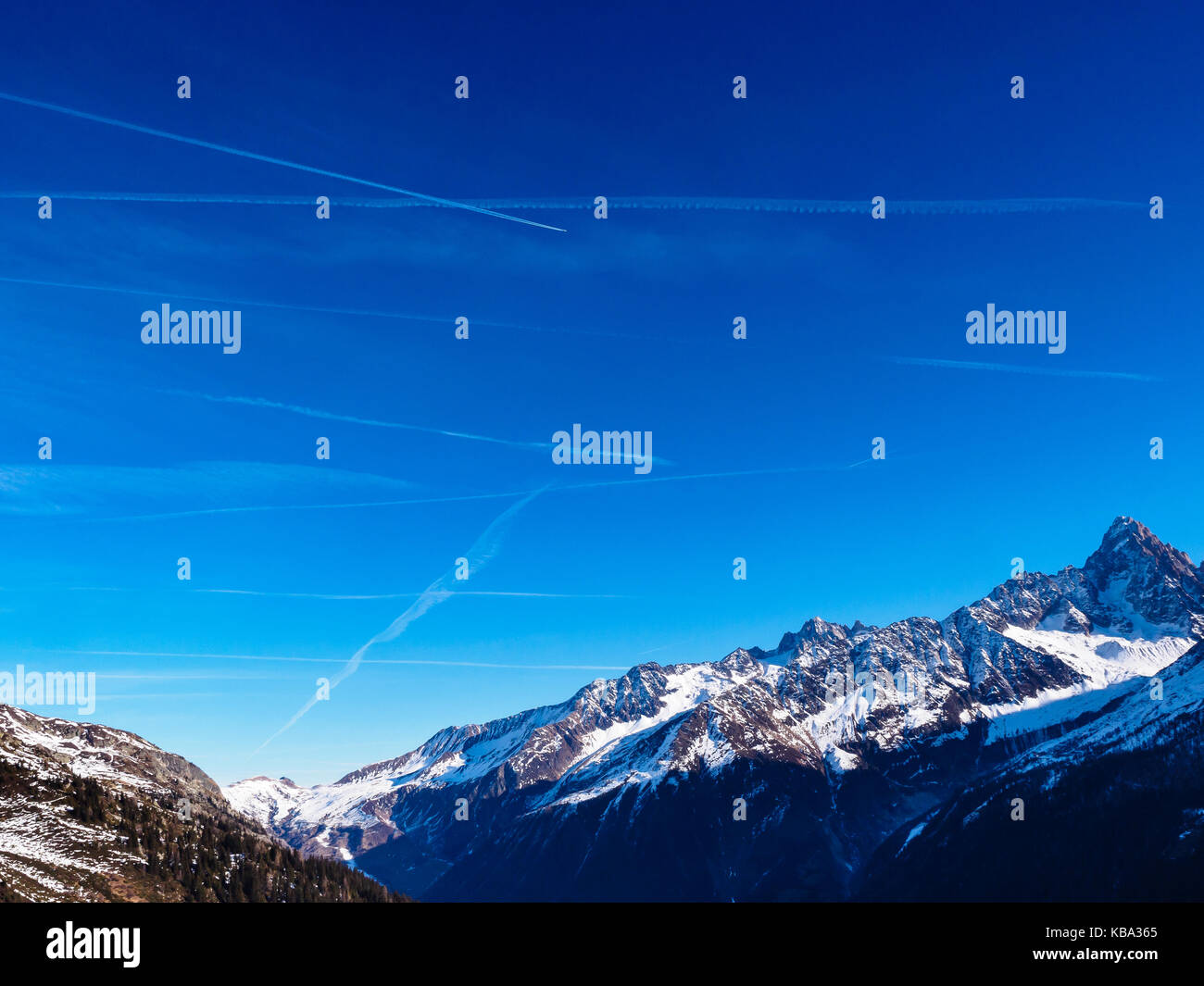 Many jet airplane contrails in clear blue sky above high peaks of ...