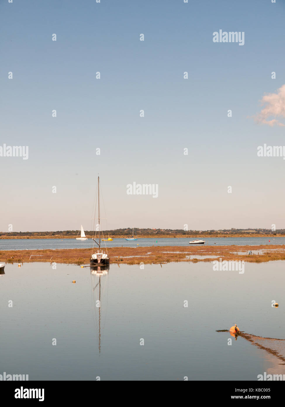 boat moored in estuary scene with mast reflected in water blue sky ...
