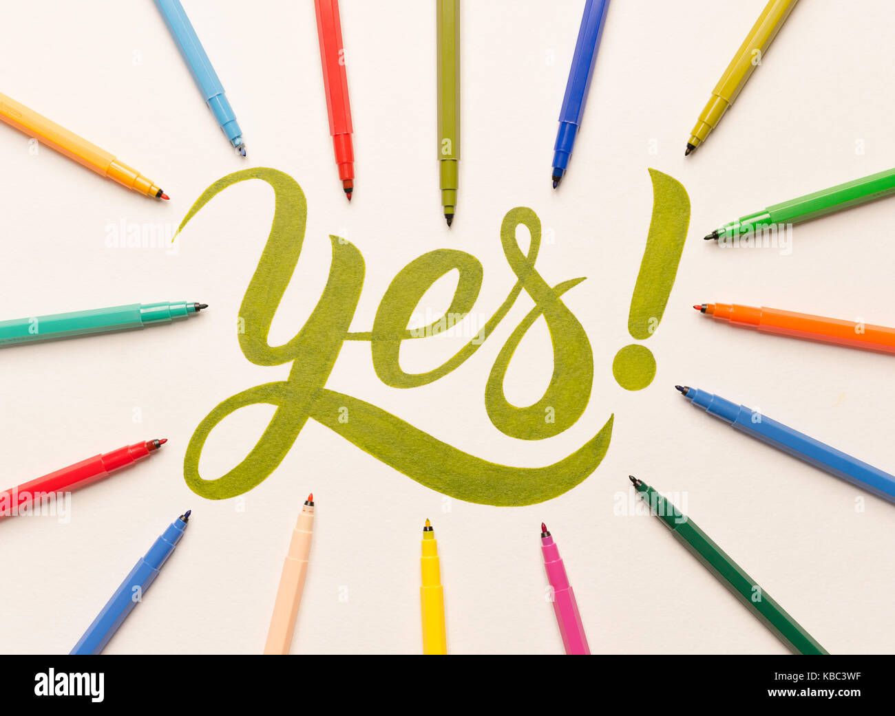 Green hand drawing phrase YES on white sheet with green markers. Top ...