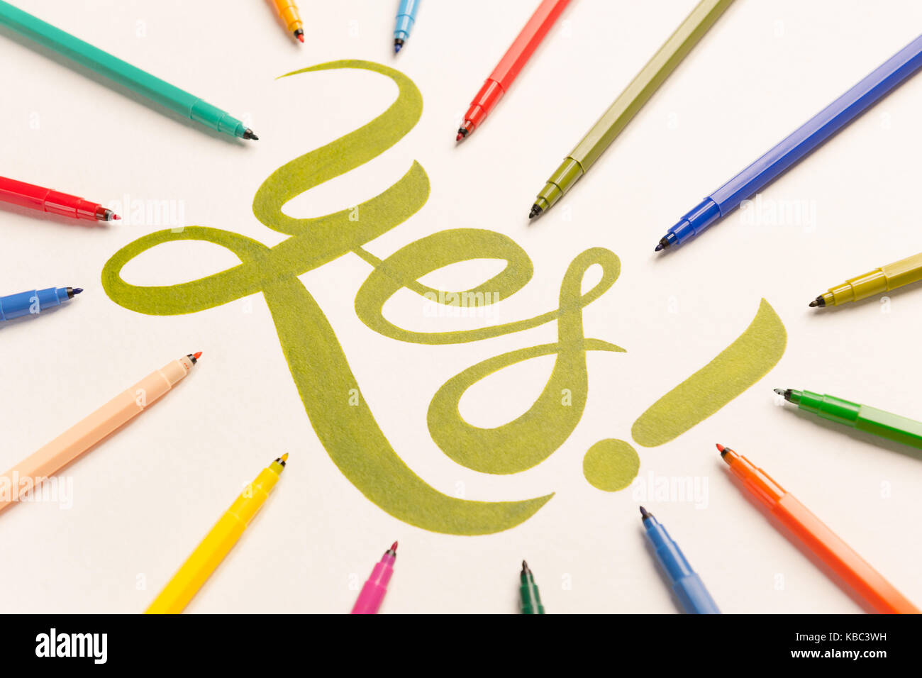 Green hand drawing phrase YES on white sheet with green markers. Top ...