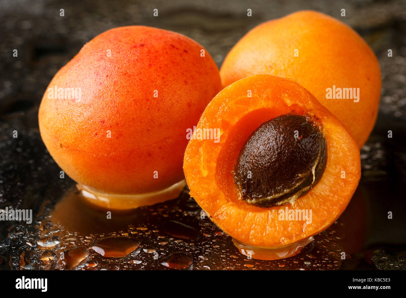 Close up of two whole and one half sliced apricot fruits with the stone ...