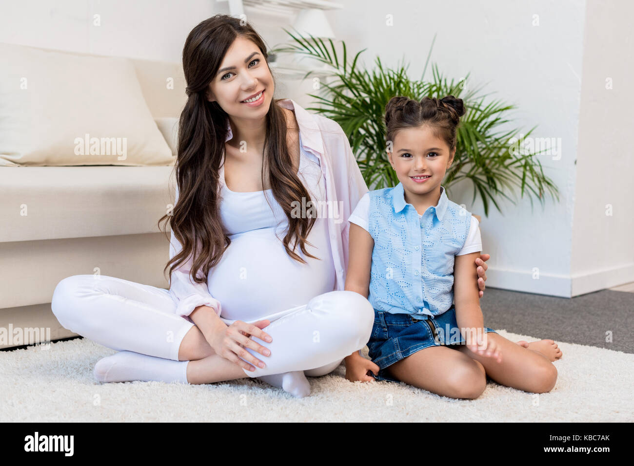 Pregnant woman with daughter sitting on rug Stock Photo - Alamy