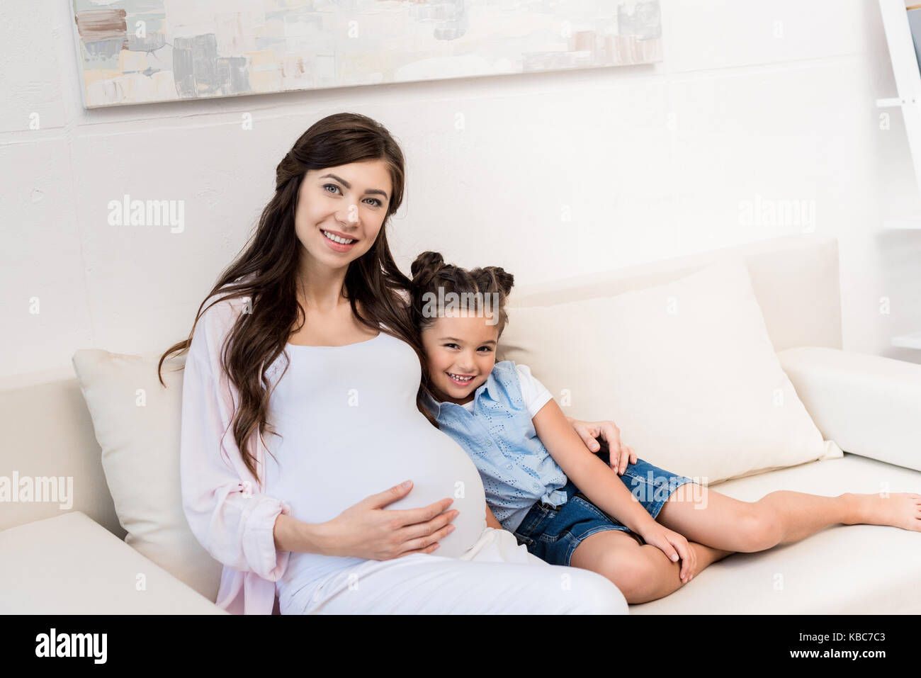Girl and pregnant mother hugging on couch Stock Photo - Alamy