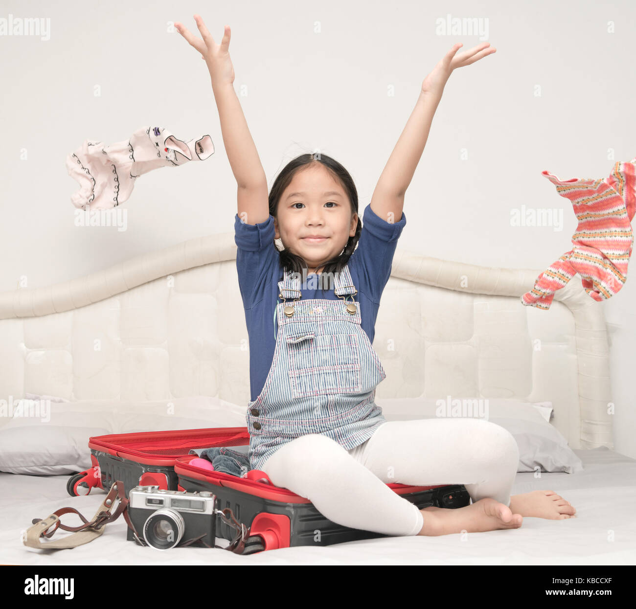 Happy cute girl throwing clothes and sit on suitcase, prepare travel ...