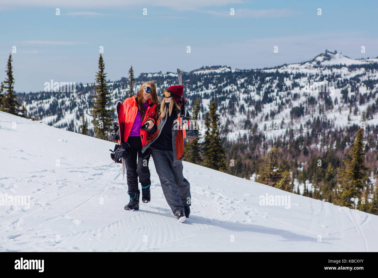 Two young women with ski and snowboard on ski holiday in mountains ...