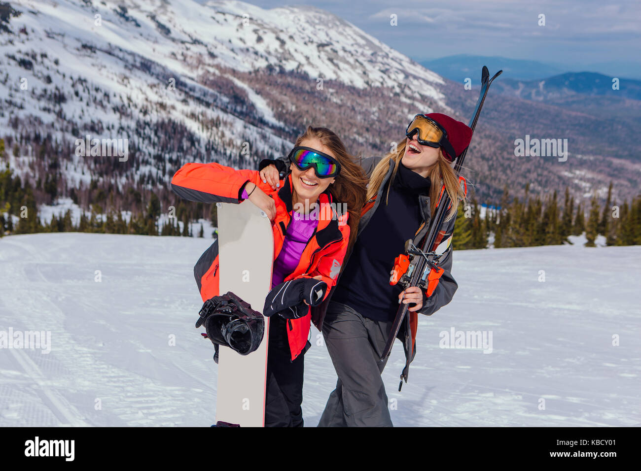 Two young women with ski and snowboard on ski holiday in mountains ...