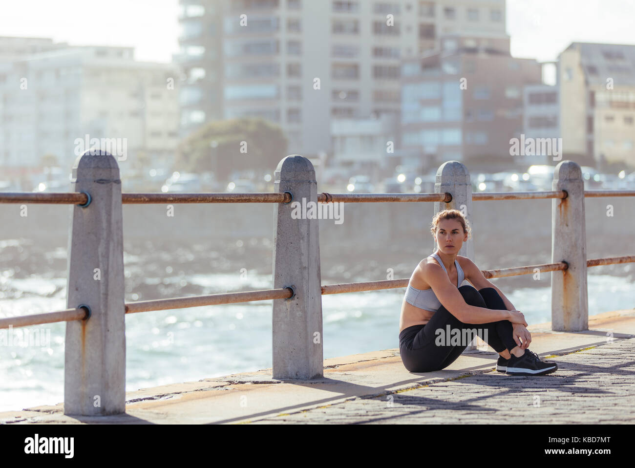 Female runner taking break after fitness training outdoors by the sea ...