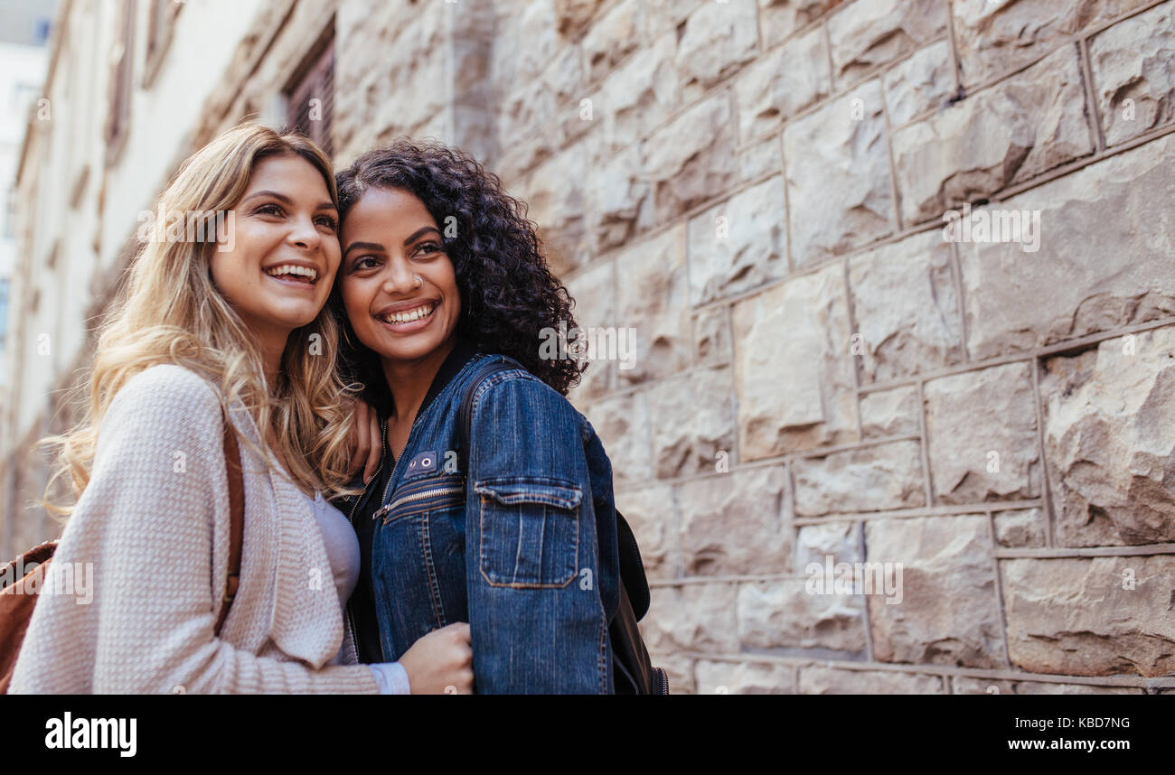 Young women standing together beside a stone wall. Two smiling women ...