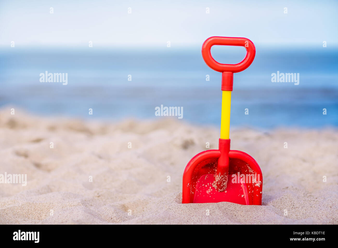 Red and yellow plastic childrens toy shovel on a beautiful white sand ...