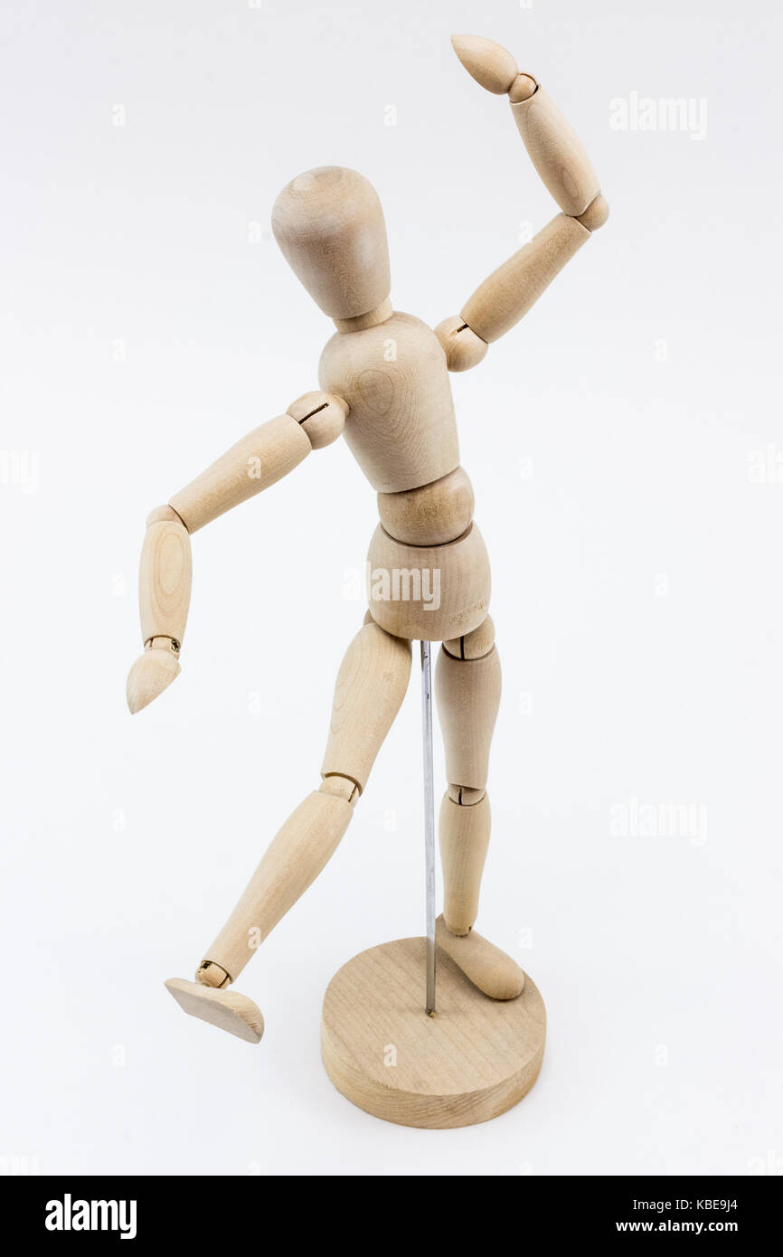 A wooden mannequin in a dance pose, on it's stand, on a white surface ...