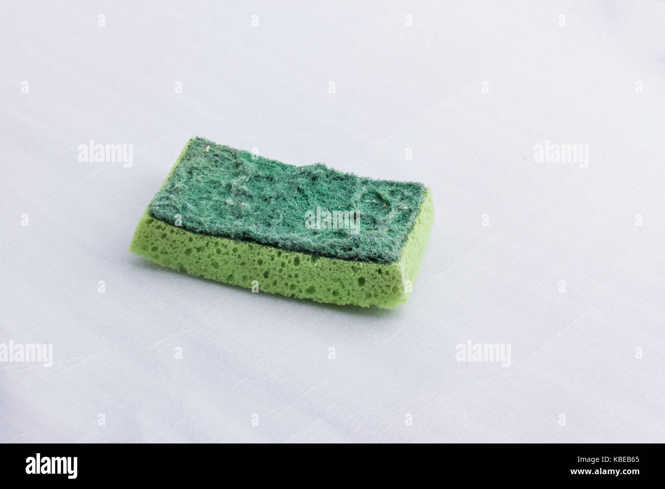 A green used kitchen sponge, with a hard and a soft surface, on a white ...