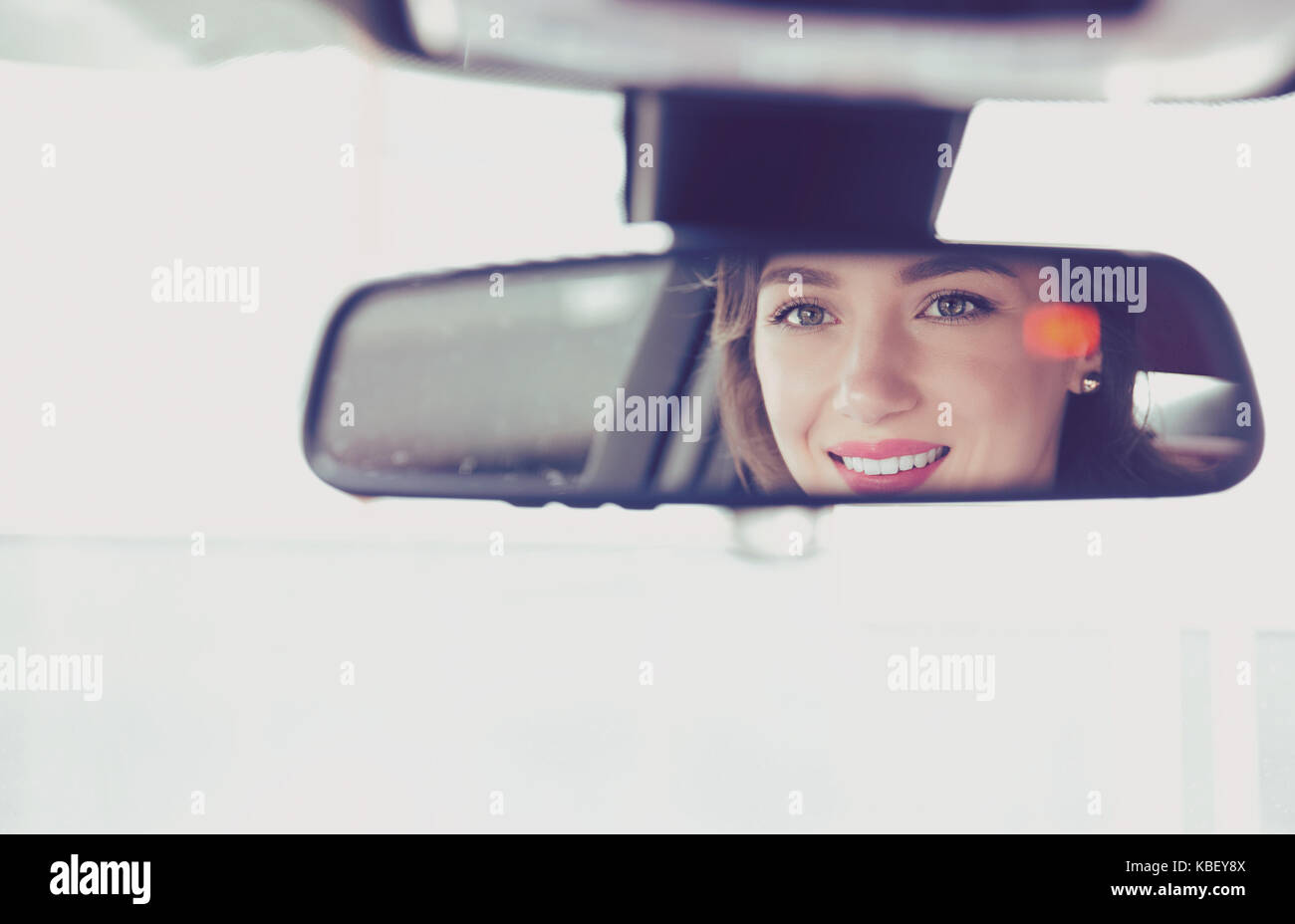 Young cheerful woman driving a car, rear view, reflexion of face in a ...