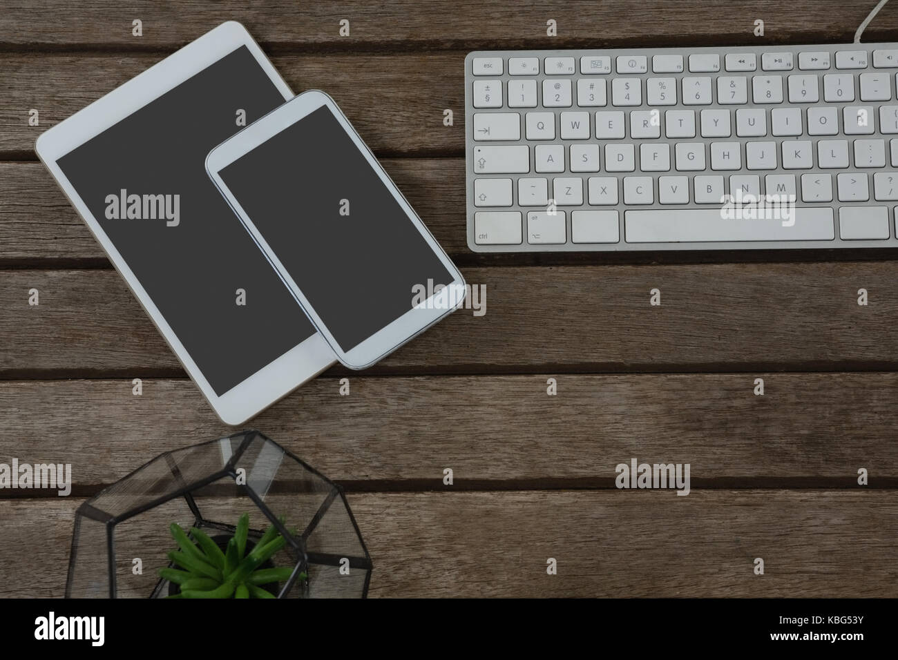 Overhead of digital tablet, mobile phone, pot plant and keyboard on ...