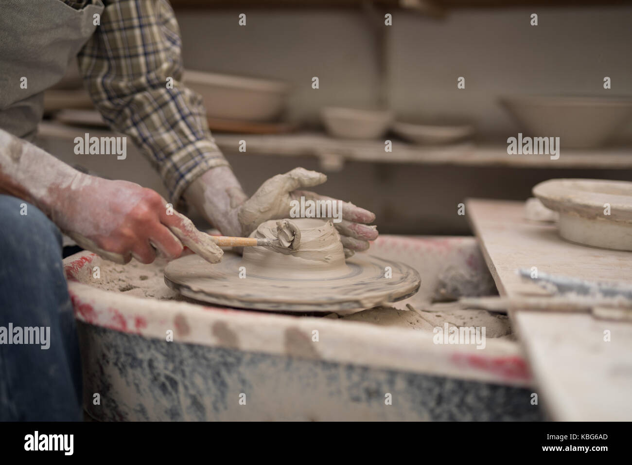 Mid section of male potter molding plate with hand tool in pottery ...