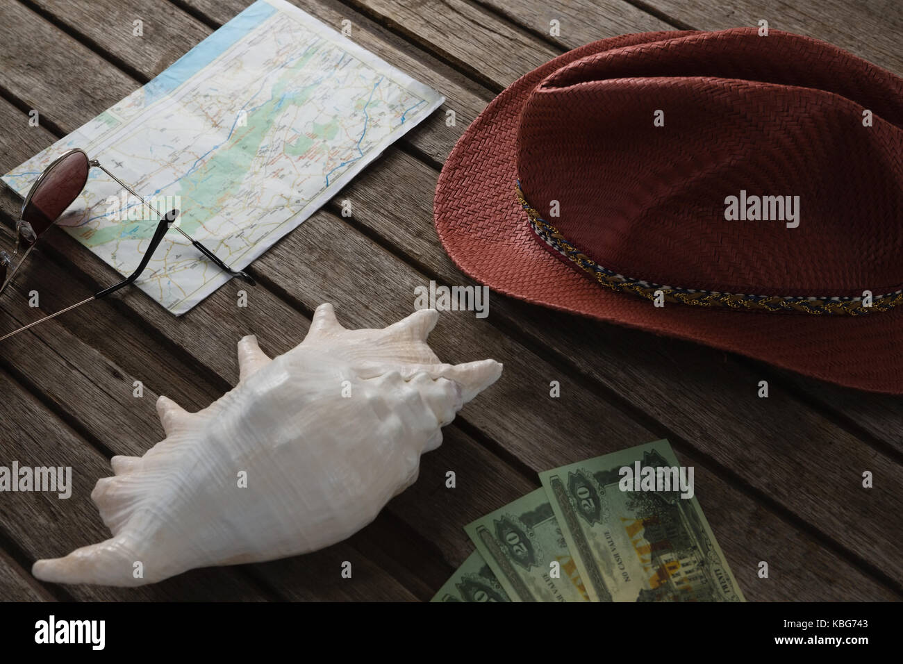 Close-up of map, hat, seashell, currency notes and sunglasses on wooden ...