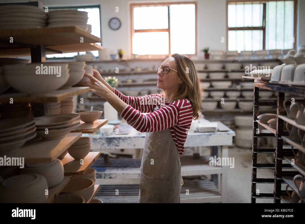 Female potter placing bowl in shelf at pottery workshop Stock Photo - Alamy