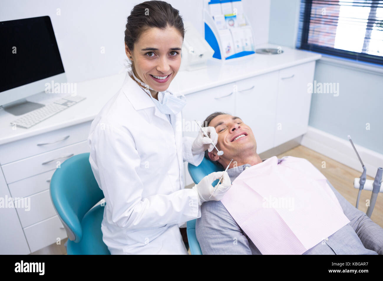 Portrait of dentist holding equipment while standing by patient at ...