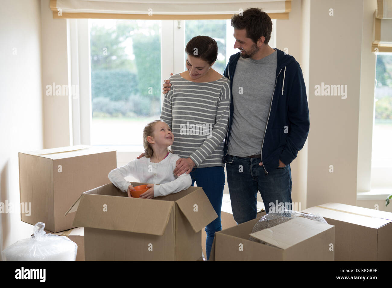 Parents and daughter opening cardboard boxes in living room at home ...