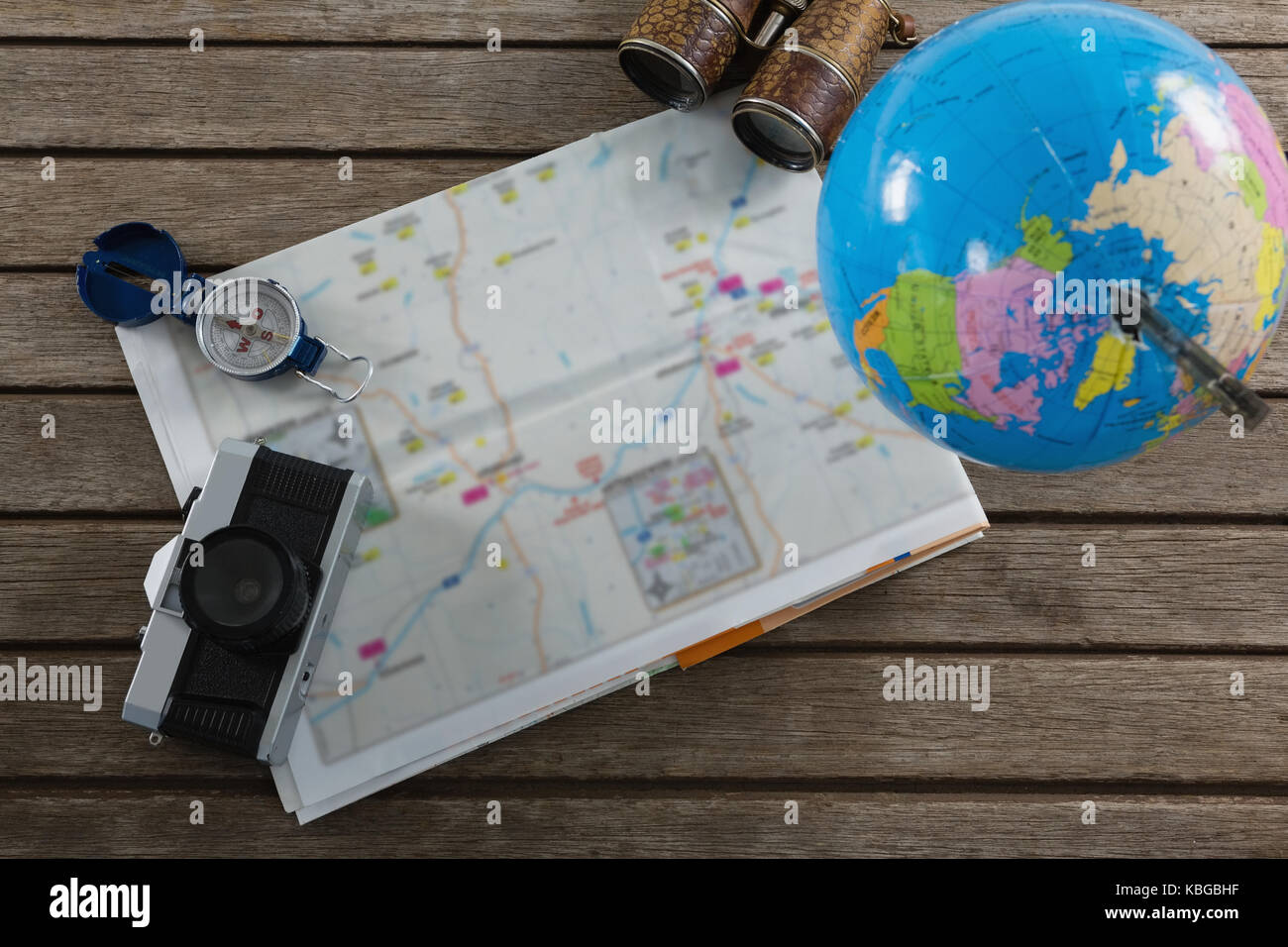 Overhead of camera, binoculars, globe, map and compass on wooden plank ...
