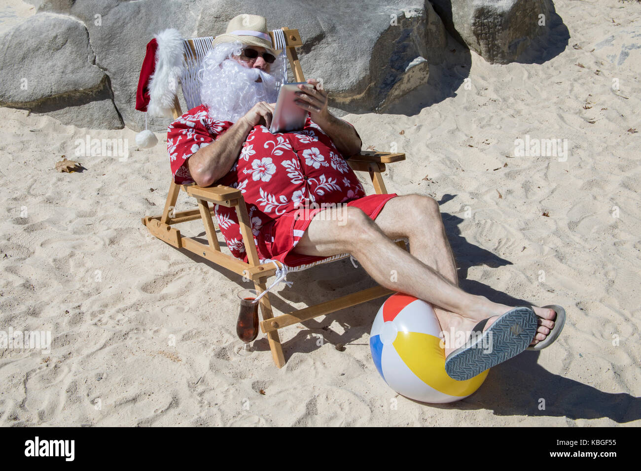 Santa Claus in red swimming trunks ans Hawaiian shirt lounging on sandy ...