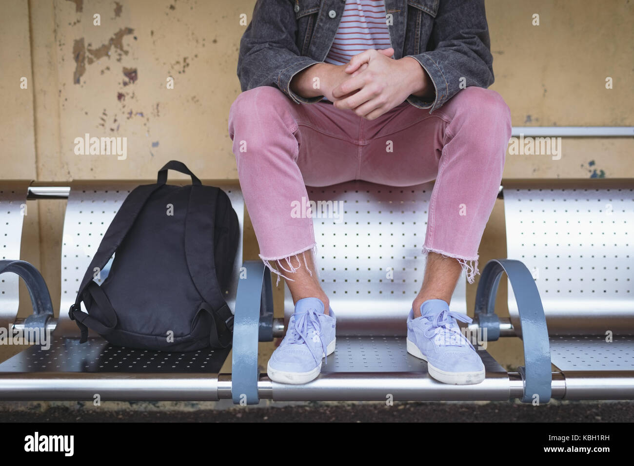 Low section of man sitting on bench at railway station Stock Photo - Alamy