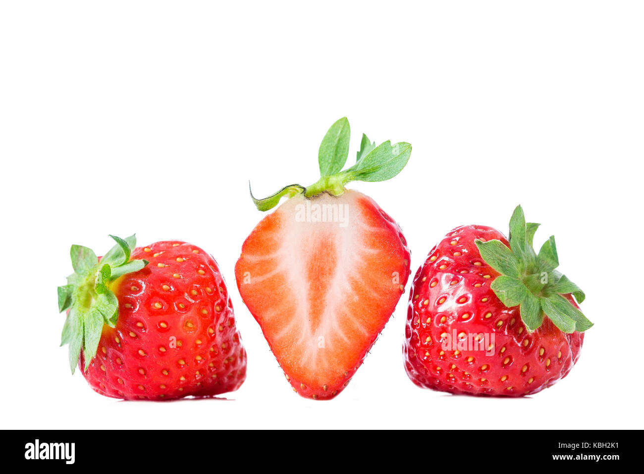Isolated strawberries. Three strawberry fruits, one cut in half with ...