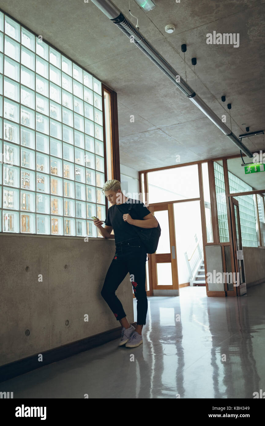 University male student using mobile phone in the corridor of college ...