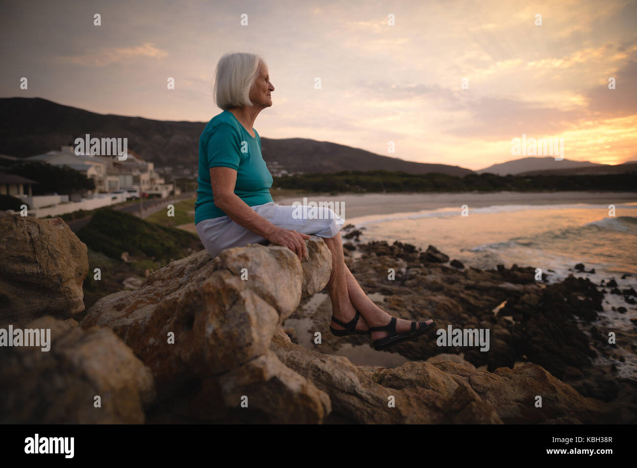 Senior woman sitting on seaside rocks during dusk Stock Photo - Alamy