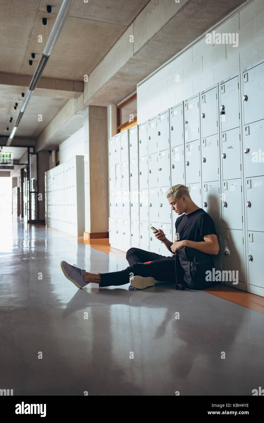 University male student using mobile phone in the corridor of college ...
