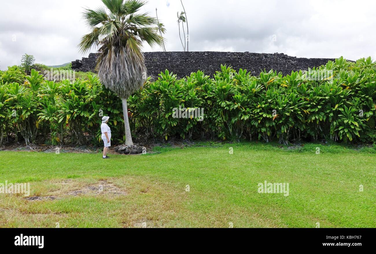 Woman standing near Piilanihale heiau whose lava rocks tower above her ...