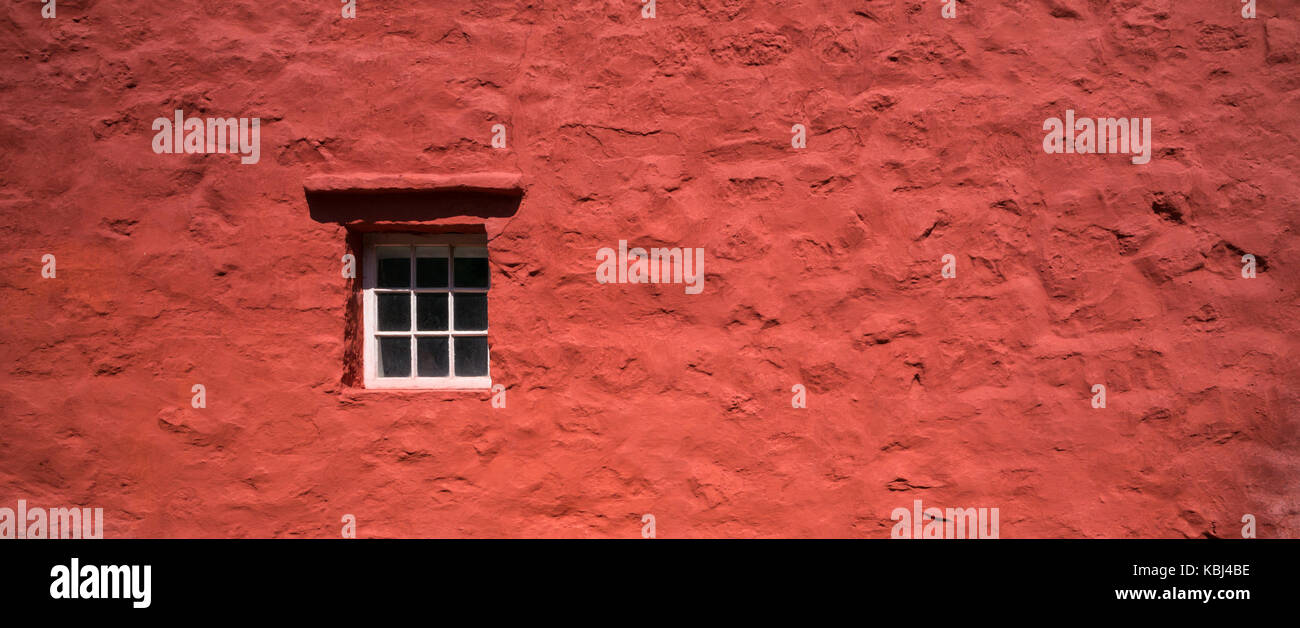 Red painted rendered stone wall of farmhouse with single window, St ...