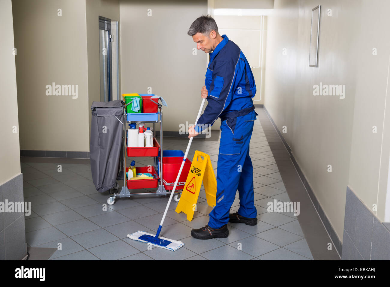 Full Length Of Mature Male Worker With Broom Cleaning Corridor Stock