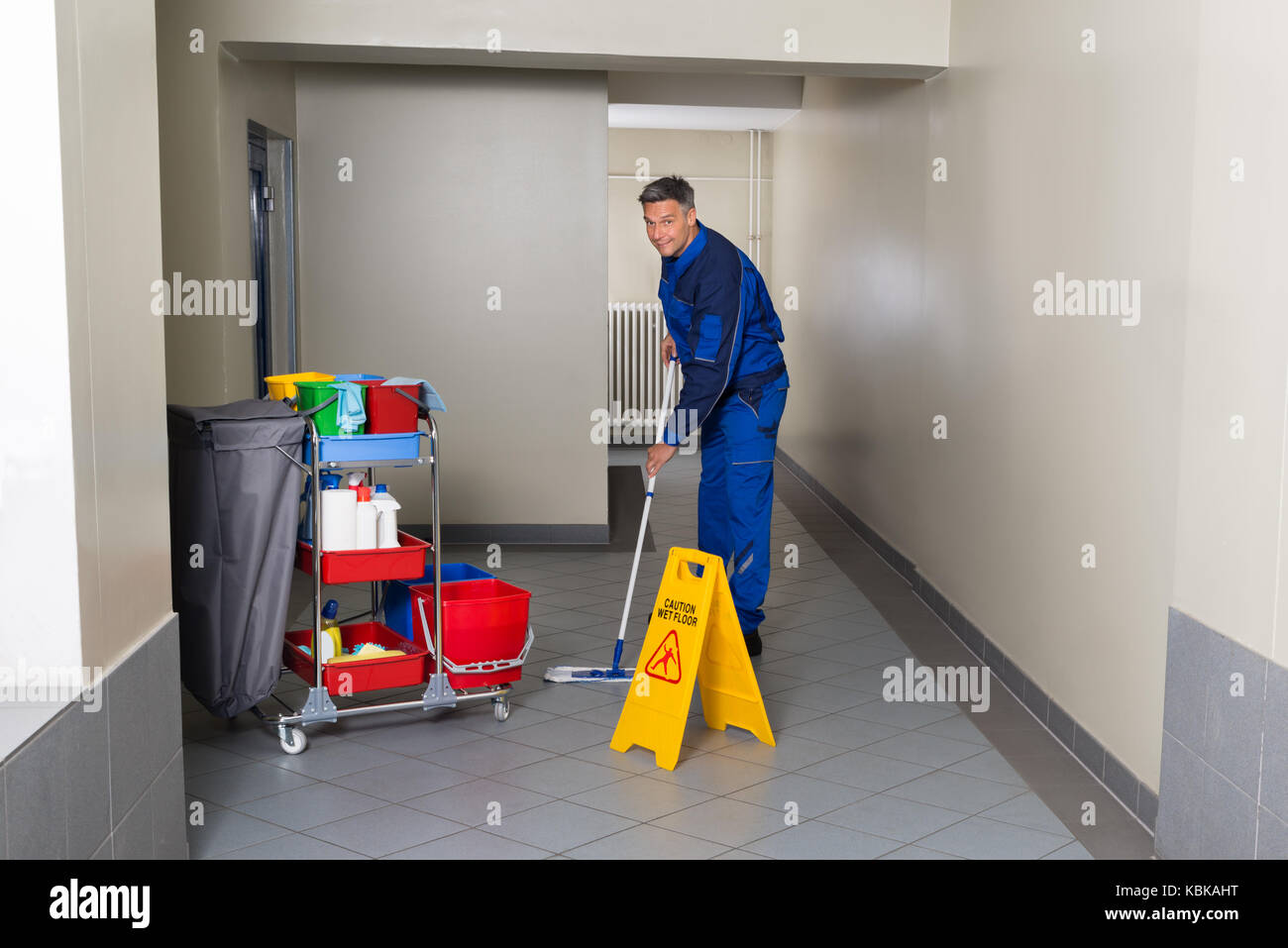 Full length of mature male worker with broom cleaning corridor Stock ...