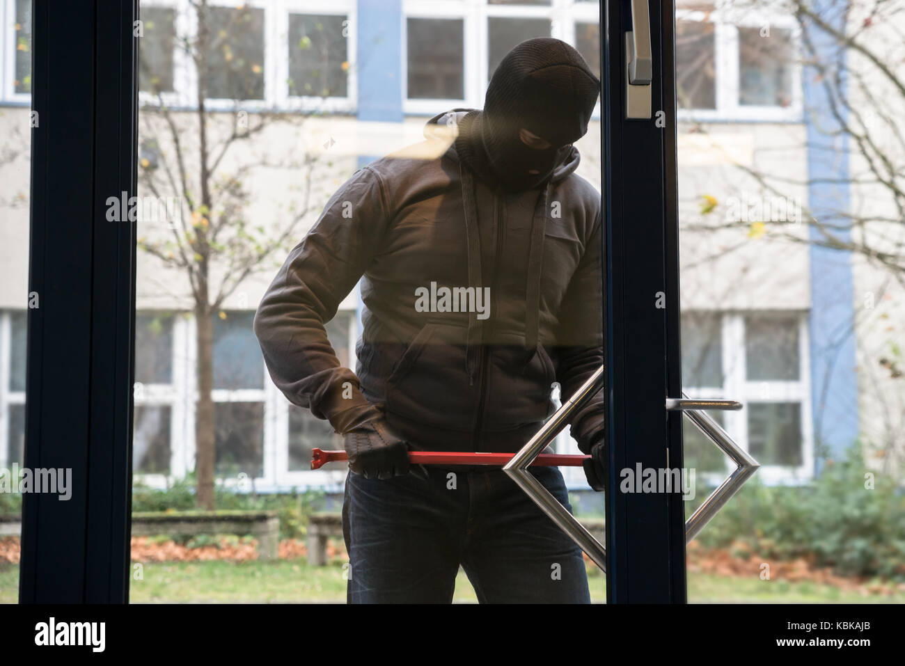 Full length of hooded man using crowbar to open glass door Stock Photo ...