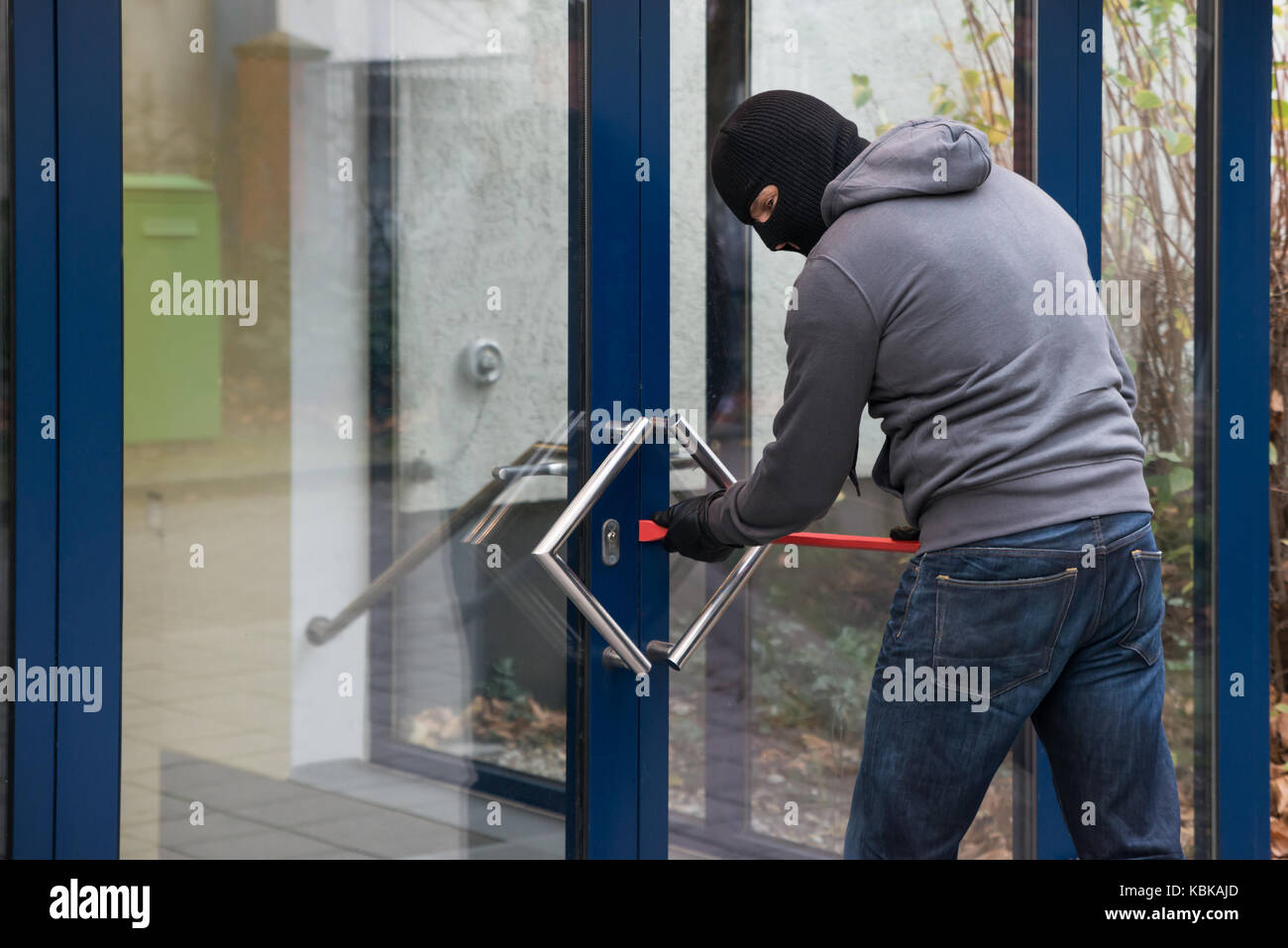 Hooded man using crowbar to open glass door Stock Photo - Alamy