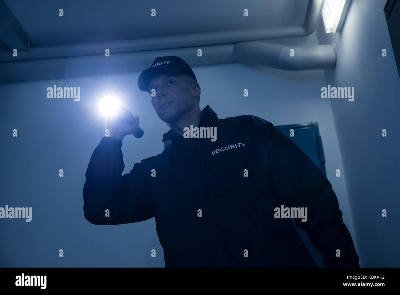 Mature security guard searching with flashlight in office building ...