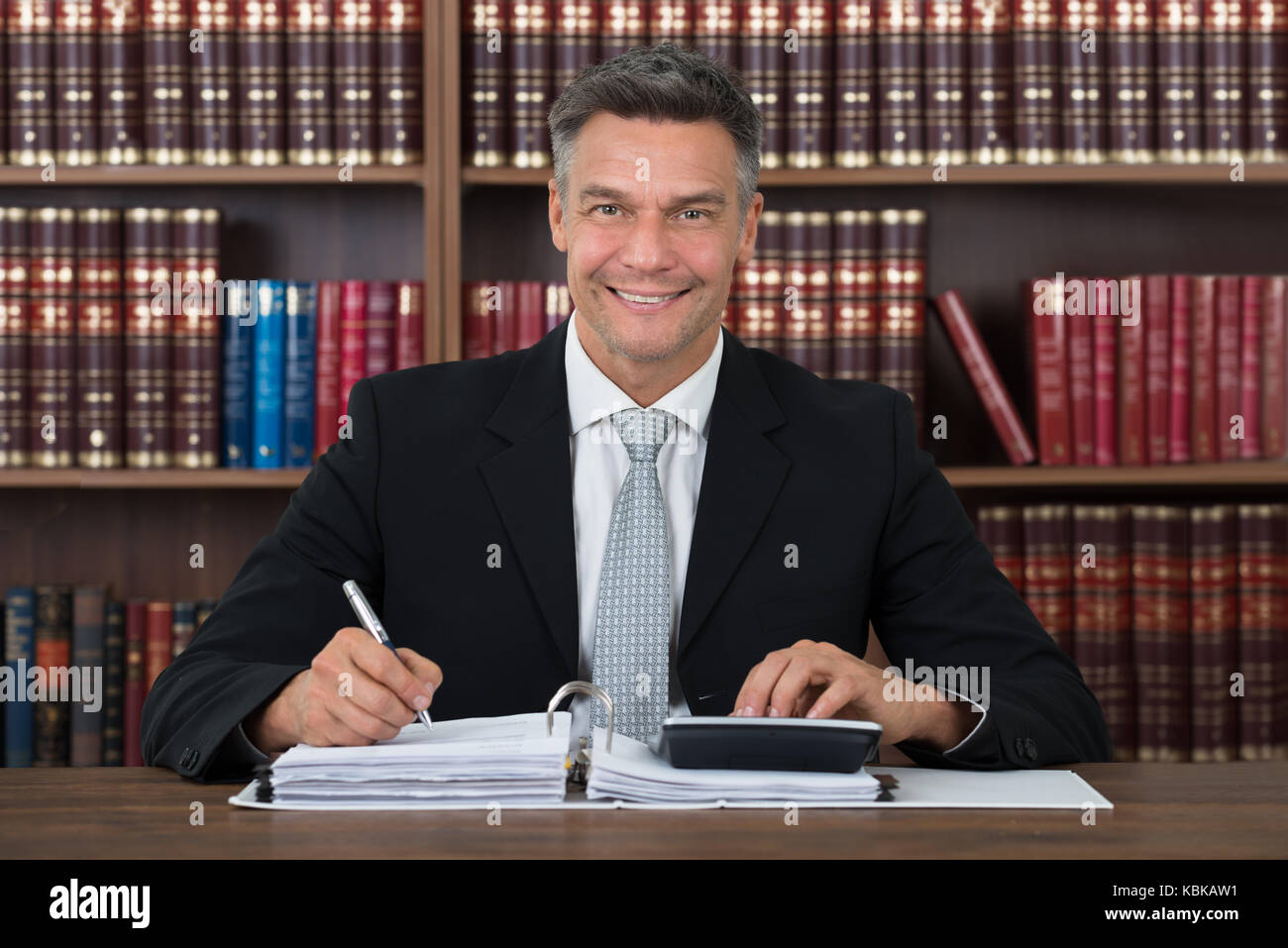 Portrait of happy male accountant writing on document while using ...