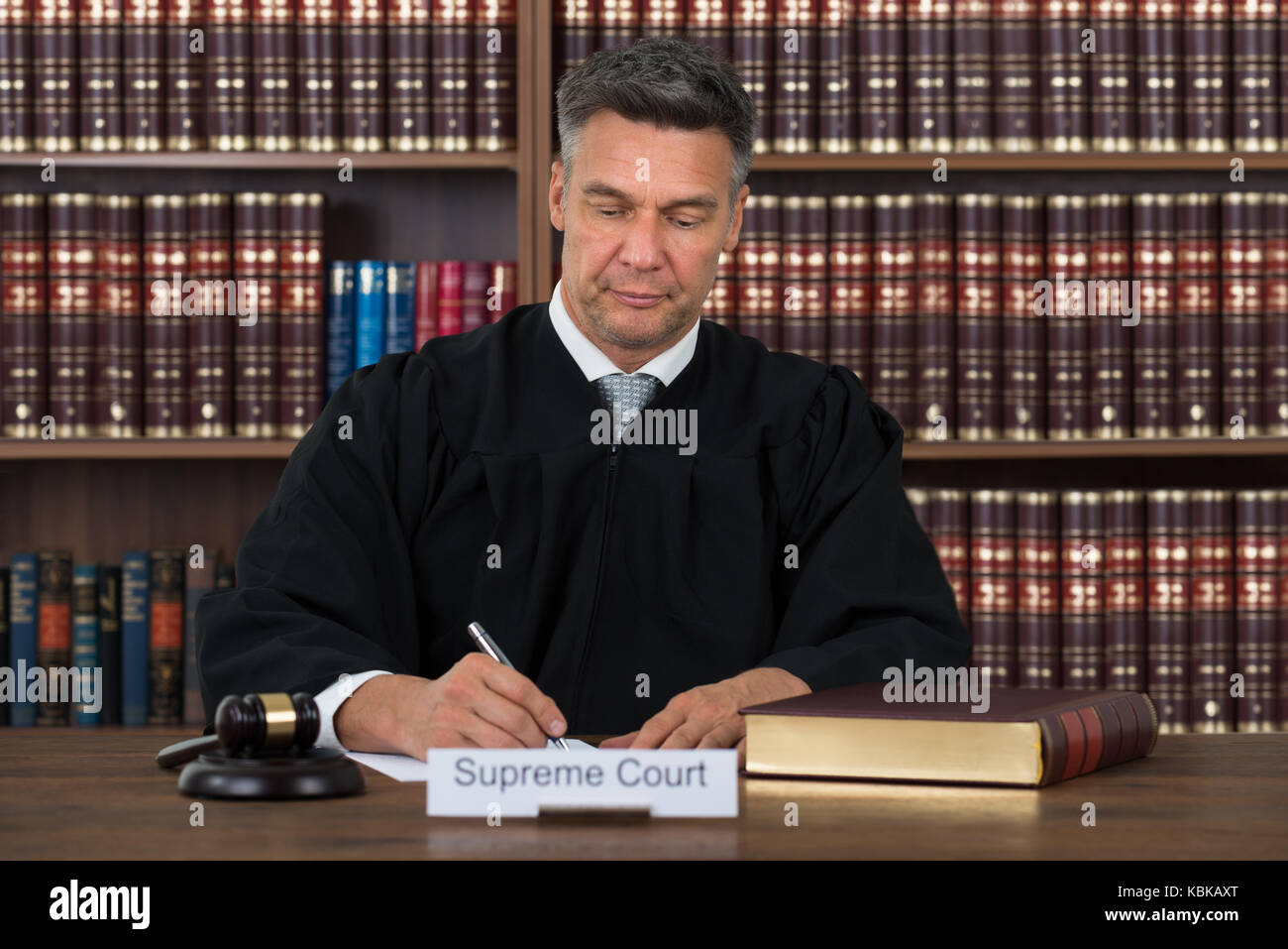 Mature male judge writing on paper at table in courtroom Stock Photo ...