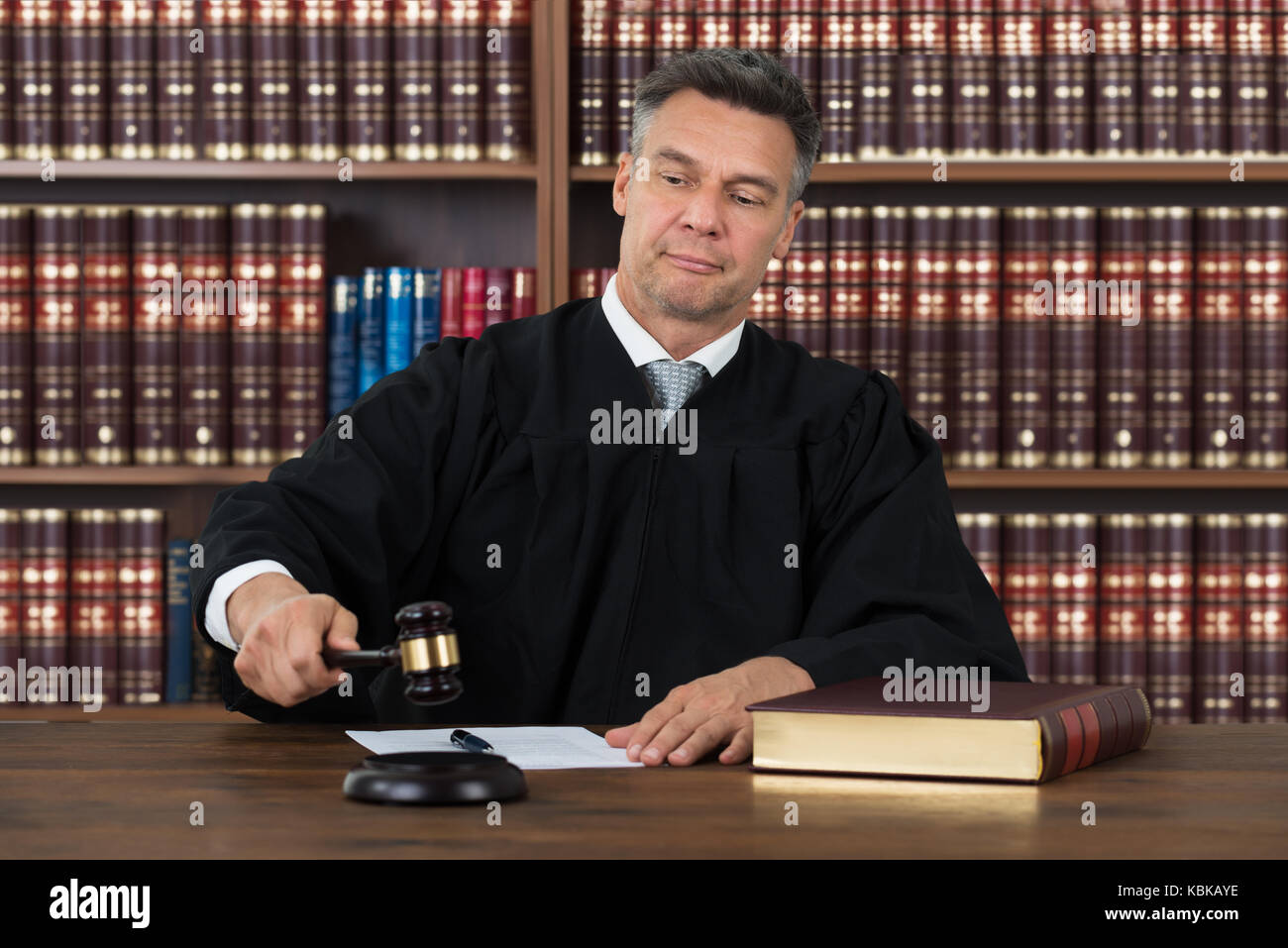 Confident mature male judge striking the gavel at table against ...
