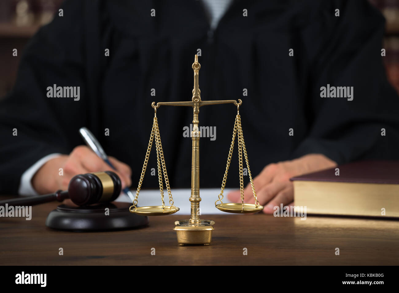 Law scales on table with judge writing in background at courtroom Stock ...