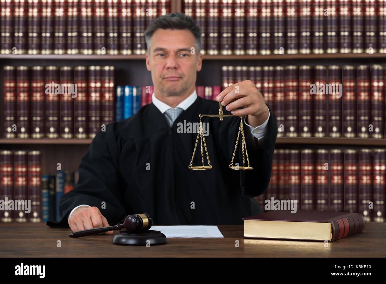 Mature male judge holding justice scale at table against bookshelf in ...