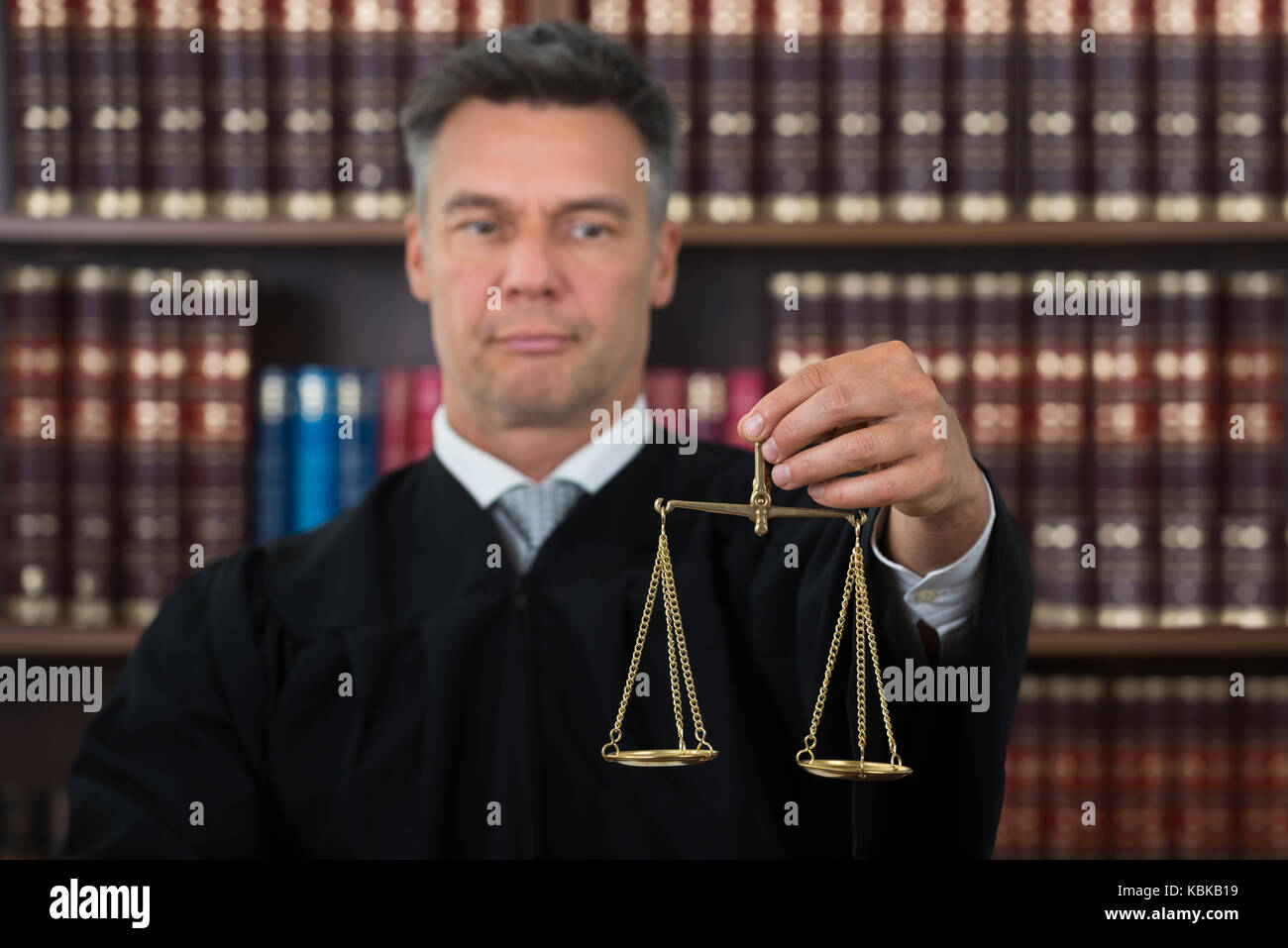 Mature male judge holding justice scale against bookshelf in courtroom ...