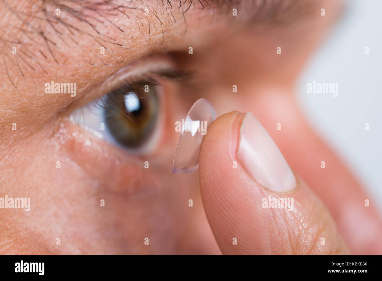 Closeup of man putting contact lens in eye over white background Stock ...