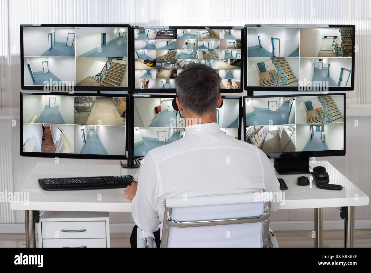 Rear view of security system operator looking at CCTV footage at desk ...