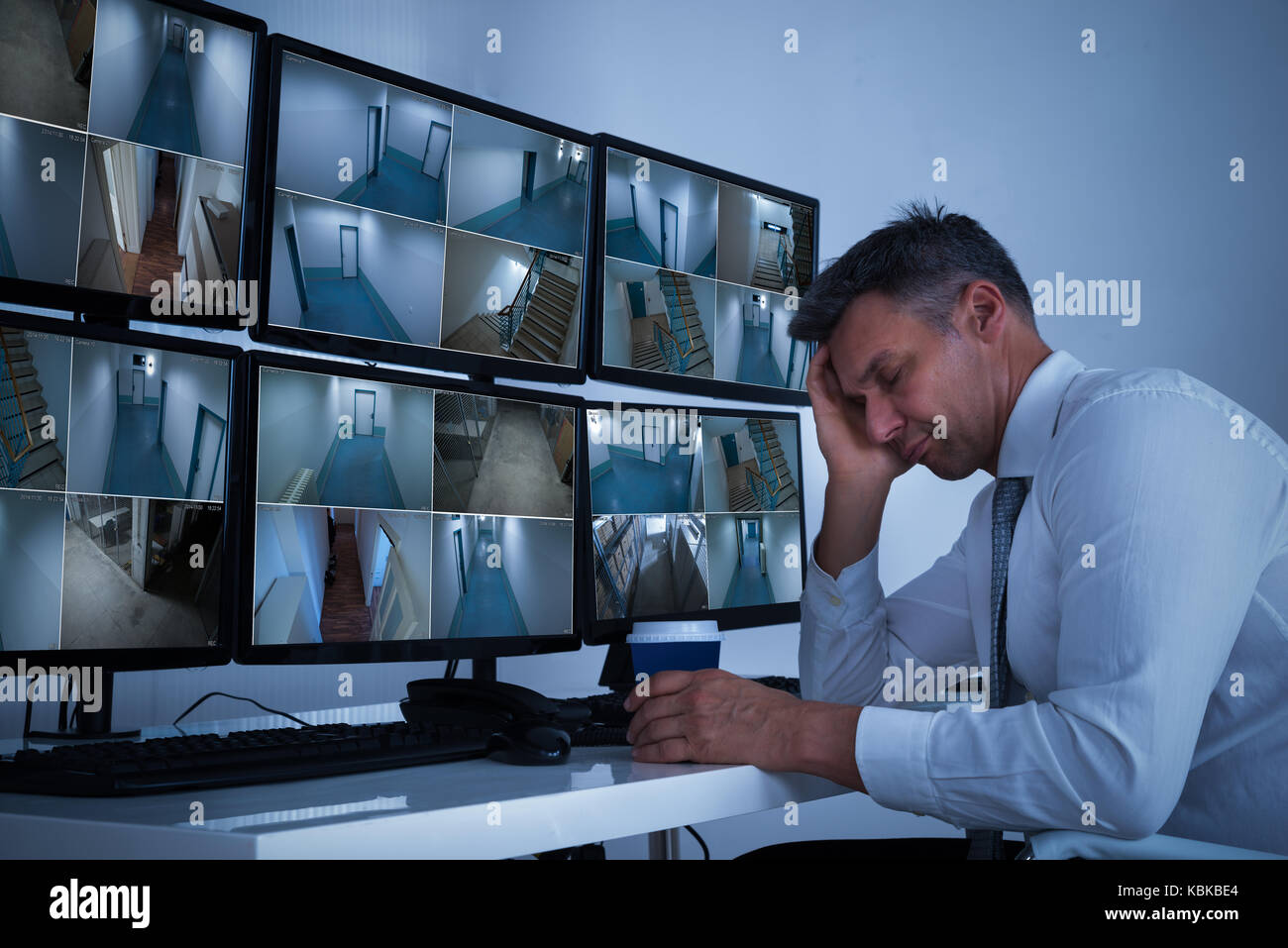 Mature security system operator sleeping while leaning on desk in ...
