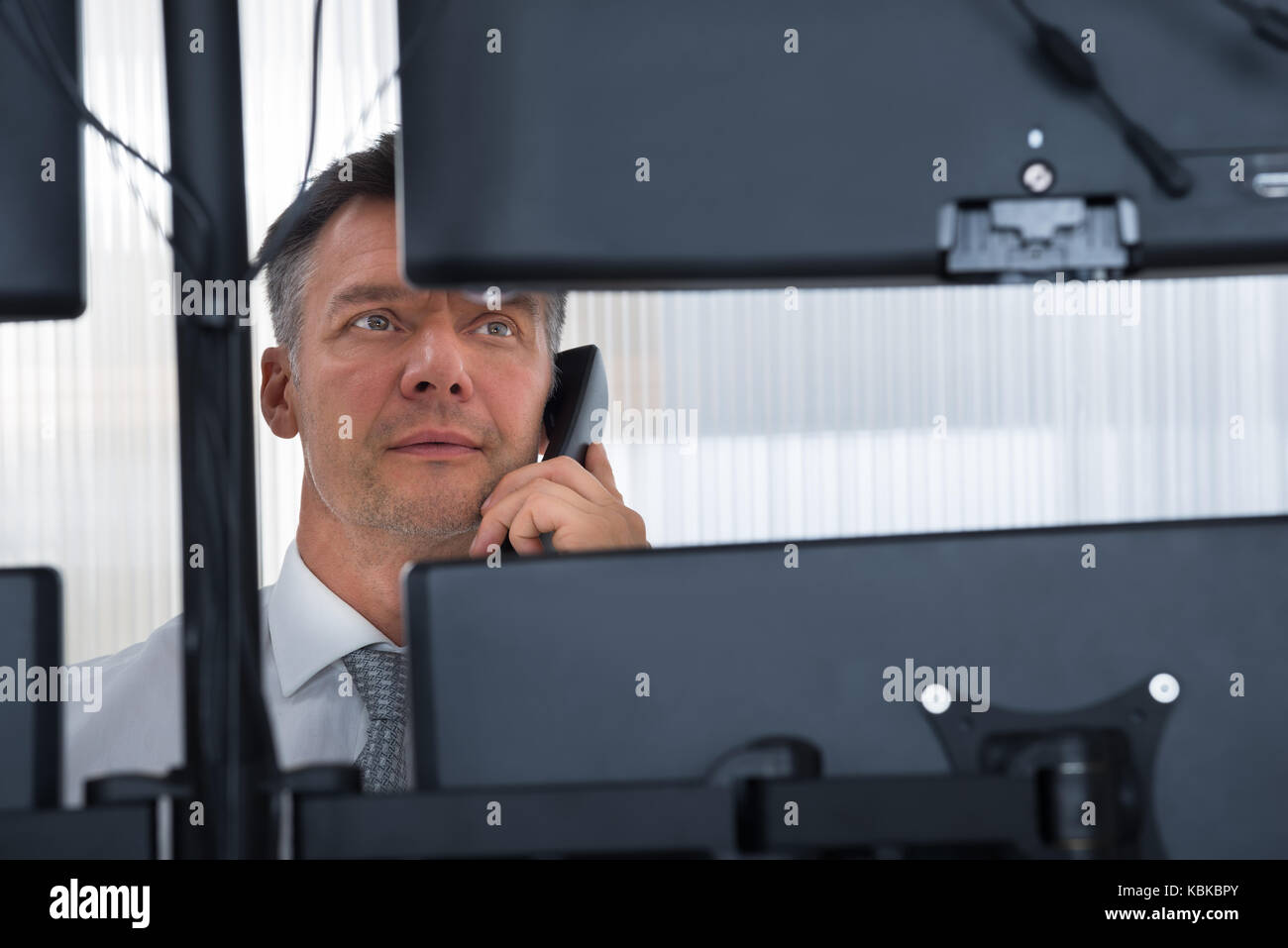 Mature male stock trader using telephone while looking at multiple ...