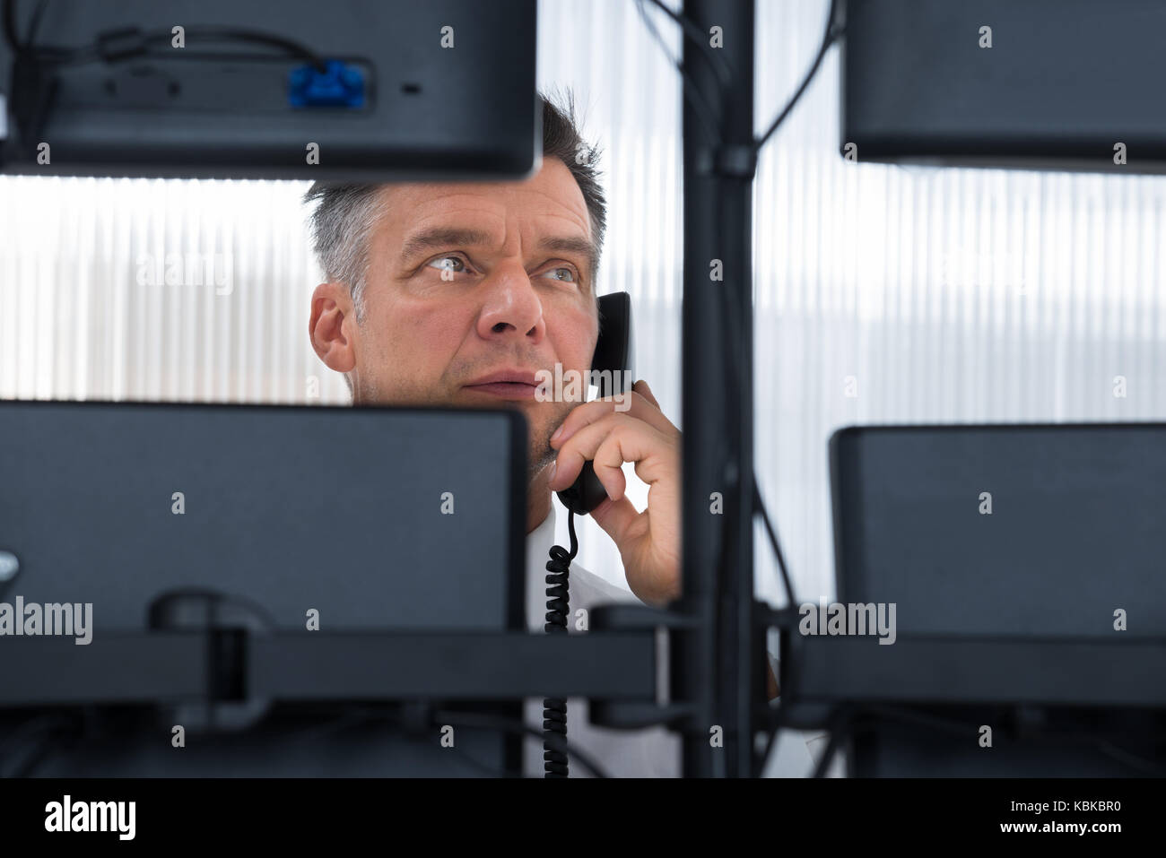 Mature male stock trader using telephone while looking at multiple ...