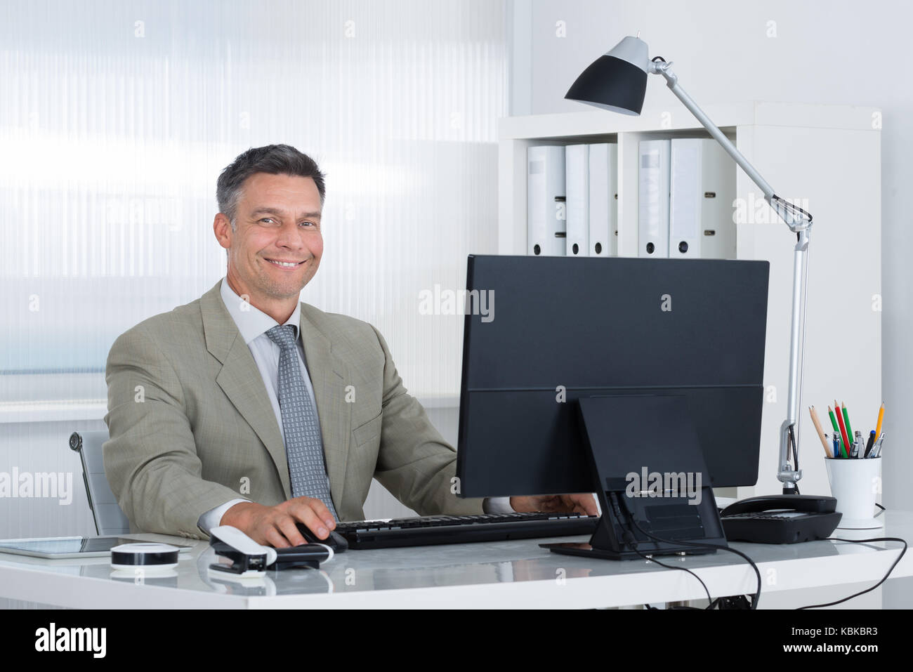 Portrait of confident businessman using computer at desk in office ...