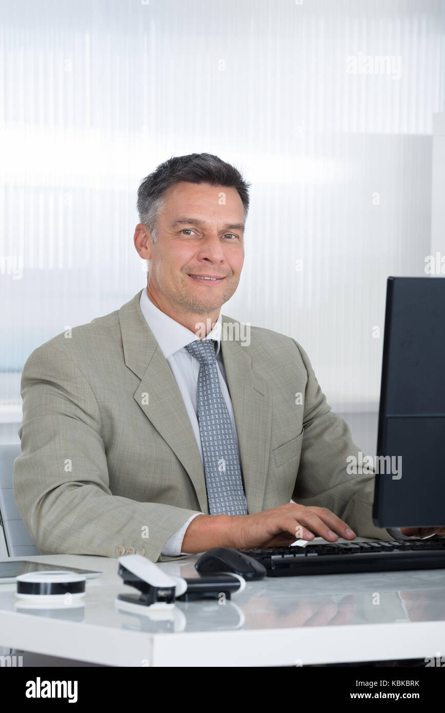 Portrait of confident businessman using computer at desk in office ...