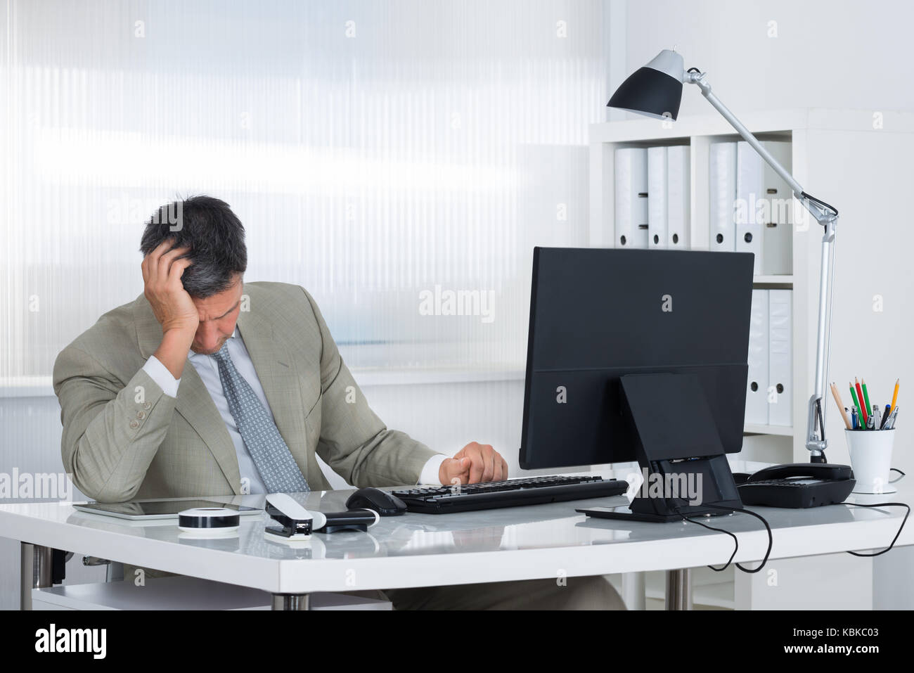Tired businessman leaning head on hand while sitting at desk in office ...